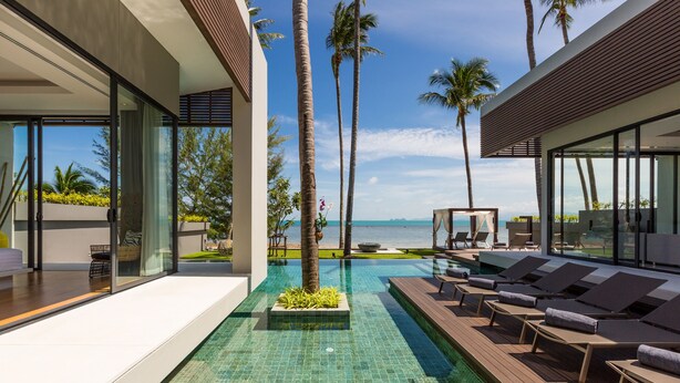 Uma área de piscina moderna com espreguiçadeiras, piscina cristalina e vista para o oceano.