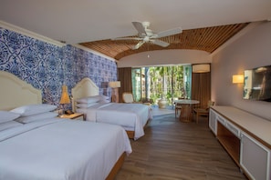 Quarto de hotel com duas camas, ventoinha no teto, televisão e vista para palmeiras.