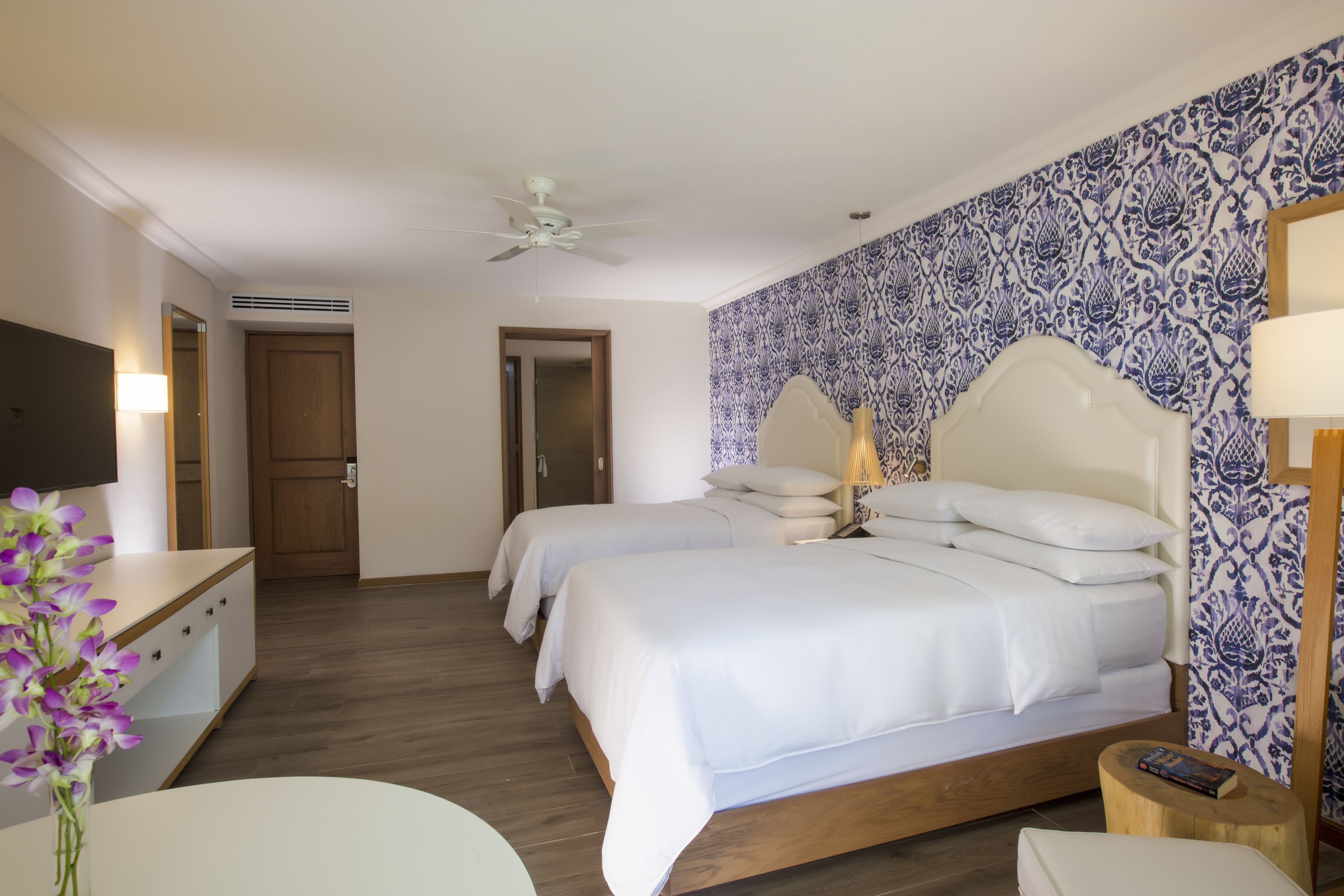 Quarto de hotel com duas camas, televisão, escrivaninha e um painel decorativo.