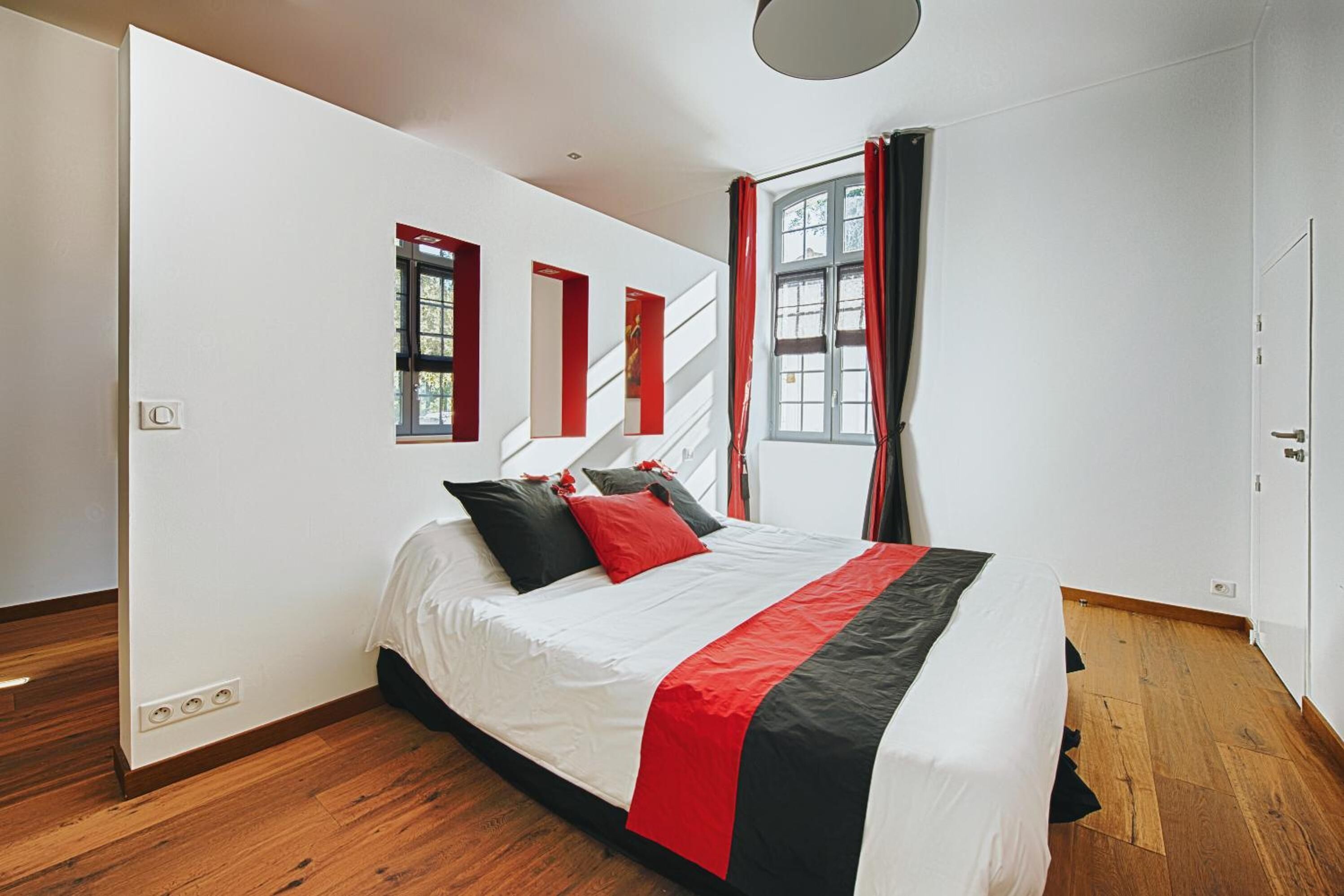 Quarto moderno com uma cama grande, uma escada e uma janela com cortinas vermelhas.