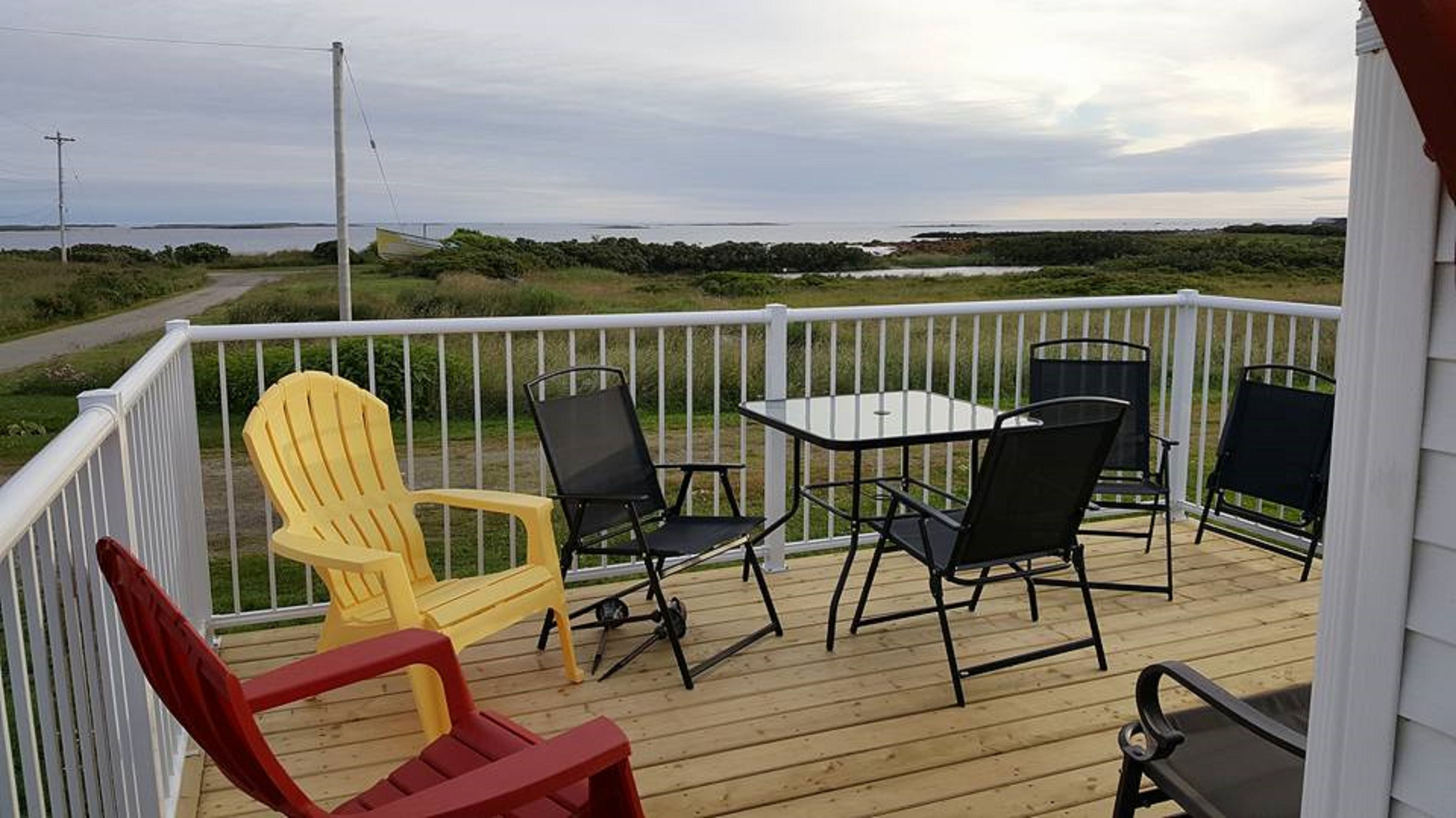 Um deck de madeira com mobiliário externo, incluindo cadeiras e uma mesa, com vista para um corpo d'água.