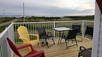 Um deck de madeira com mobiliário externo, incluindo cadeiras e uma mesa, com vista para um corpo d'água.