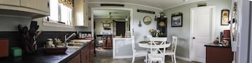 Cozinha com pia, mesa de jantar com cadeiras e uma porta. Há diversos utensílios e objetos decorativos nas bancadas.
