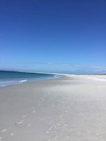 Uma praia extensa e arenosa, com ondas suaves e um céu azul límpido.