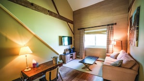 Quarto acolhedor com escrivaninha de madeira, sofá confortável, TV de tela plana e janela com cortinas.