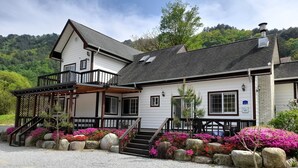 Uma casa de dois andares com varanda, alpendre coberto e entrada por uma estrada de cascalho.