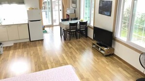 Cozinha compacta com geladeira, mesa de jantar com cadeiras, TV de tela plana e grandes janelas com vista para o exterior.
