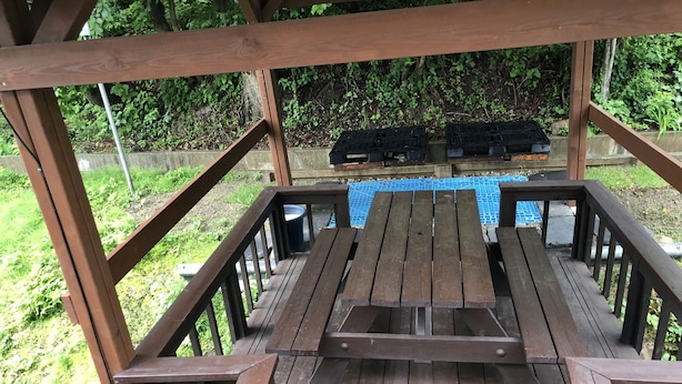 Um deck de madeira com mesas de piquenique e uma área azul com azulejos ao fundo.