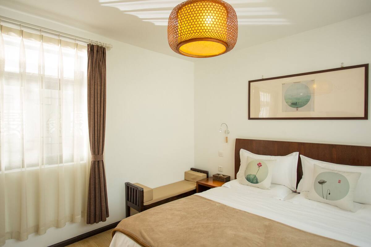 Quarto de hotel com cama, mesa de cabeceira, abajur e um quadro na parede.