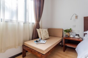 Uma cama de solteiro com estrutura de madeira, uma mesa de cabeceira com abajur, uma pequena planta e uma revista sobre a cama.