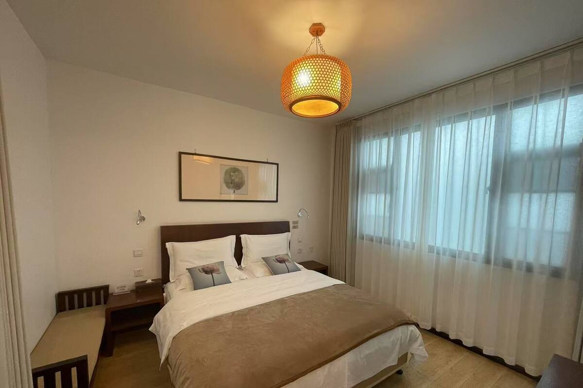 Quarto de hotel com uma cama grande, uma mesa de cabeceira, uma escrivaninha e um candeeiro suspenso.