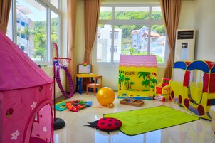Um quarto claro com uma tenda cor-de-rosa para brincar, um tapete de jogos colorido e uma grande janela com cortinas.