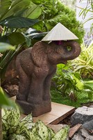 Uma estátua de pedra de um elefante com telhado cónico, colocada sobre uma plataforma rodeada por vegetação exuberante.