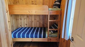 Uma cama beliche de madeira com escada, um pequeno armário e uma porta com cortina.