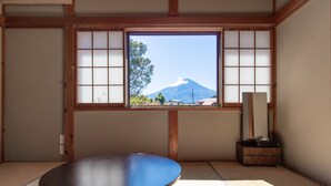 Um quarto japonês tradicional com tatames, um painel deslizante shoji, uma mesa de madeira e vista para uma montanha.