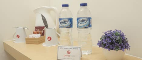 Balcão de recepção com cafeteira, duas garrafas de água mineral prim-3, uma pequena planta em vaso e uma placa com o nome e o slogan do hotel.