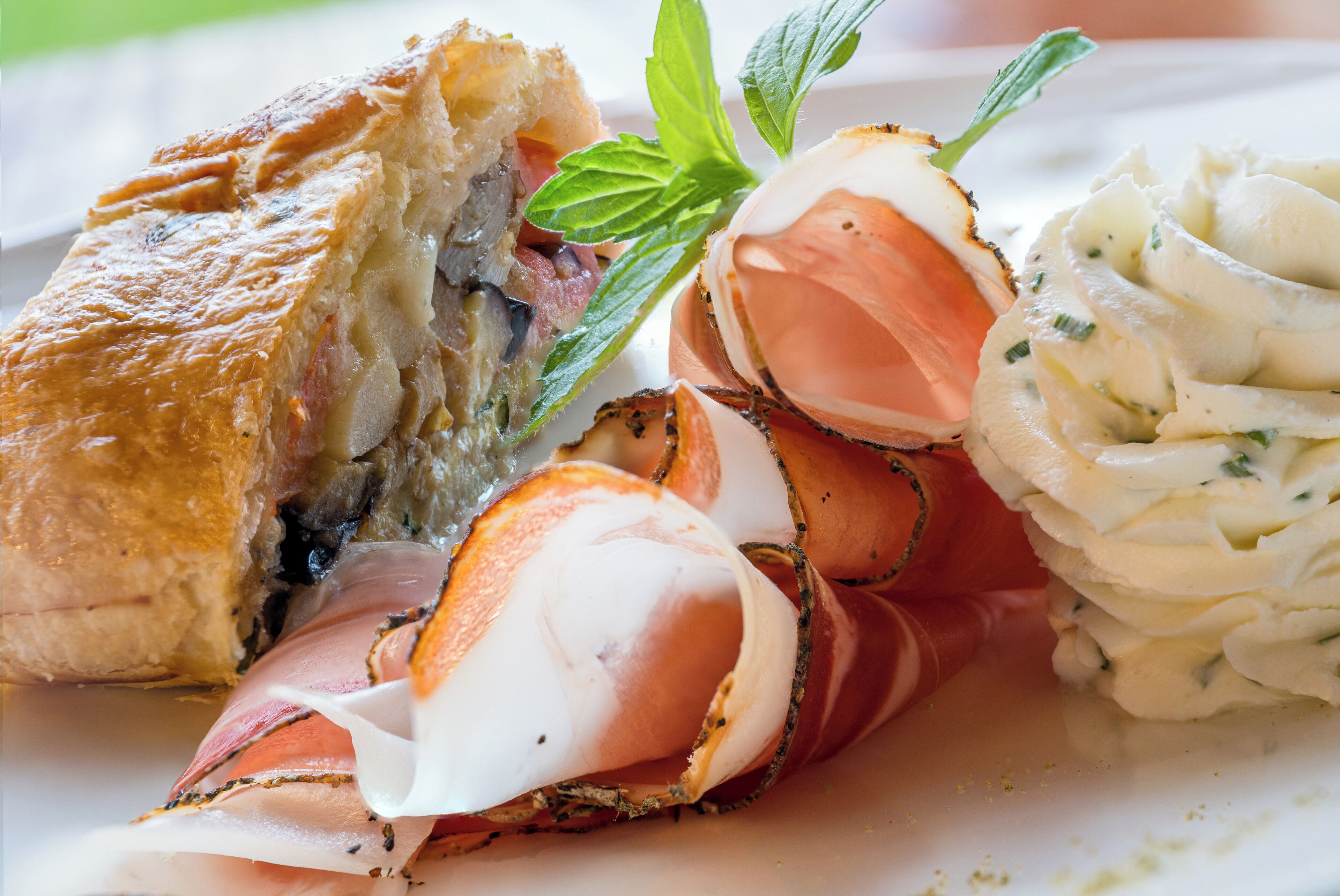 Um prato com um pastel, carne fatiada e um acompanhamento cremoso.
