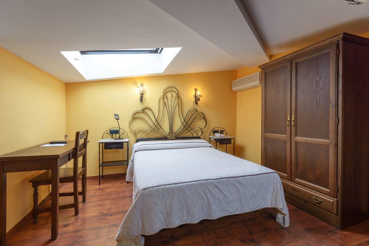 Quarto com cama, escrivaninha, cadeira, guarda-roupa e claraboia.