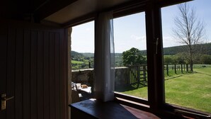 Quarto com uma grande janela que oferece vista para um campo gramado e um muro de pedra.