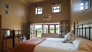 Quarto com cama, penteadeira e janela com vista para o verde.