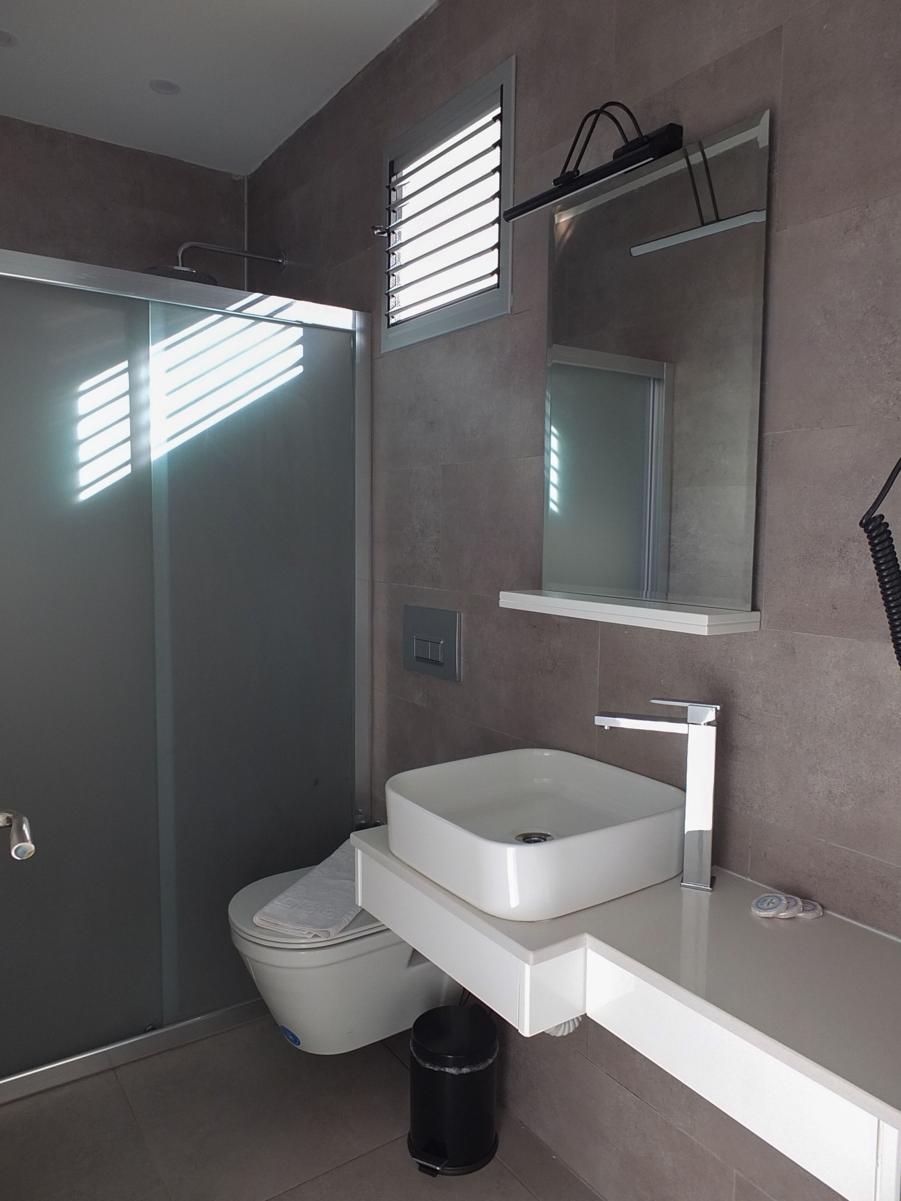 Uma casa de banho moderna com cabine de duche em vidro, lavatório branco e sanita.
