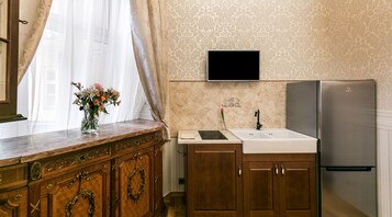 Cozinha com armários de madeira, bancada de mármore, geladeira de aço inoxidável e TV na parede.