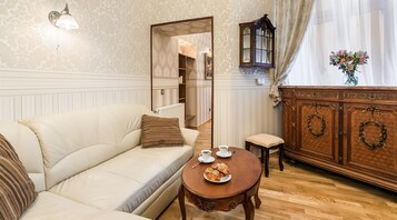 Uma sala de estar acolhedora com um sofá bege, um armário de madeira com guirlandas decorativas e uma mesa pequena com uma chávena e pastelaria.