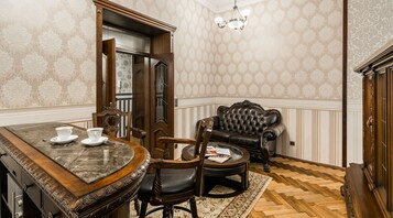 Uma área de refeições com uma mesa de mármore, cadeiras e uma chávena de café. Há um sofá de couro e um tapete estampado no chão.
