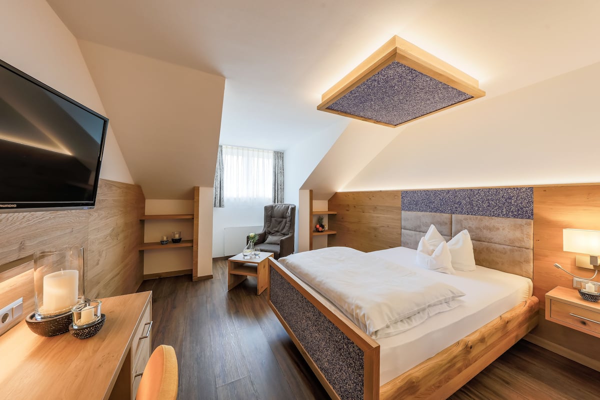 Quarto de hotel moderno com uma cama grande, uma escrivaninha com televisão de tela plana, uma cadeira e uma mesinha de centro com uma vela.
