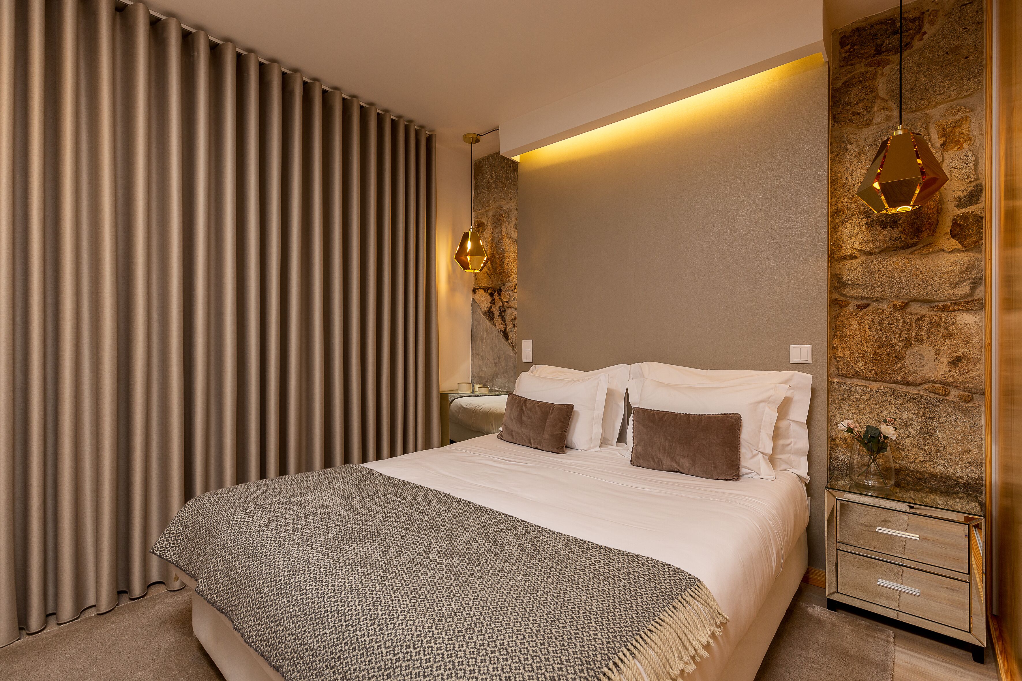 Quarto moderno com cama grande, parede de destaque em pedra e luminária pendente.