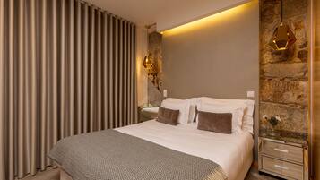 Quarto moderno com cama grande, parede de destaque em pedra e luminária pendente.