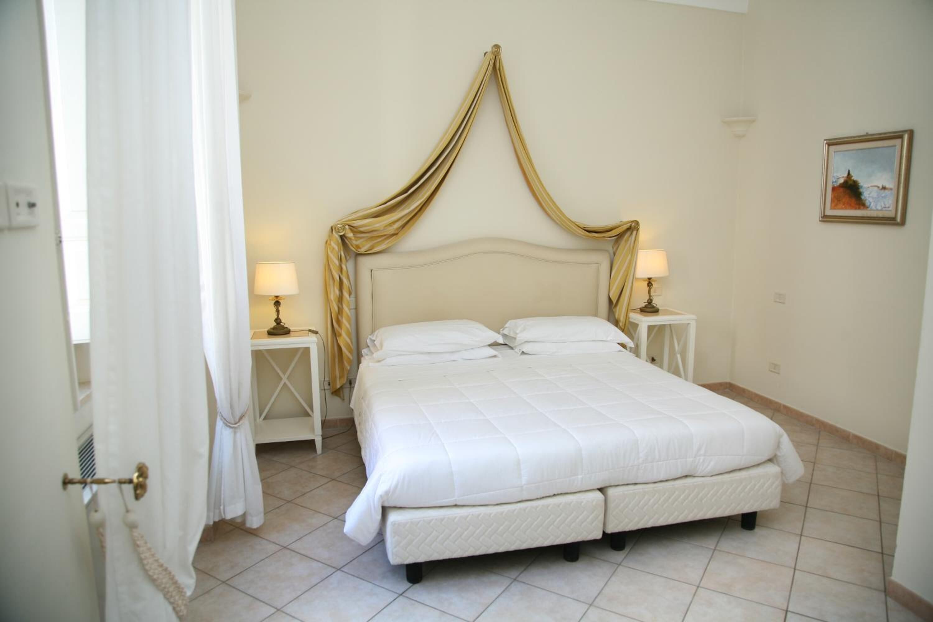 Uma cama bem arrumada com dossel, duas mesas de cabeceira com luminárias e um quadro na parede.