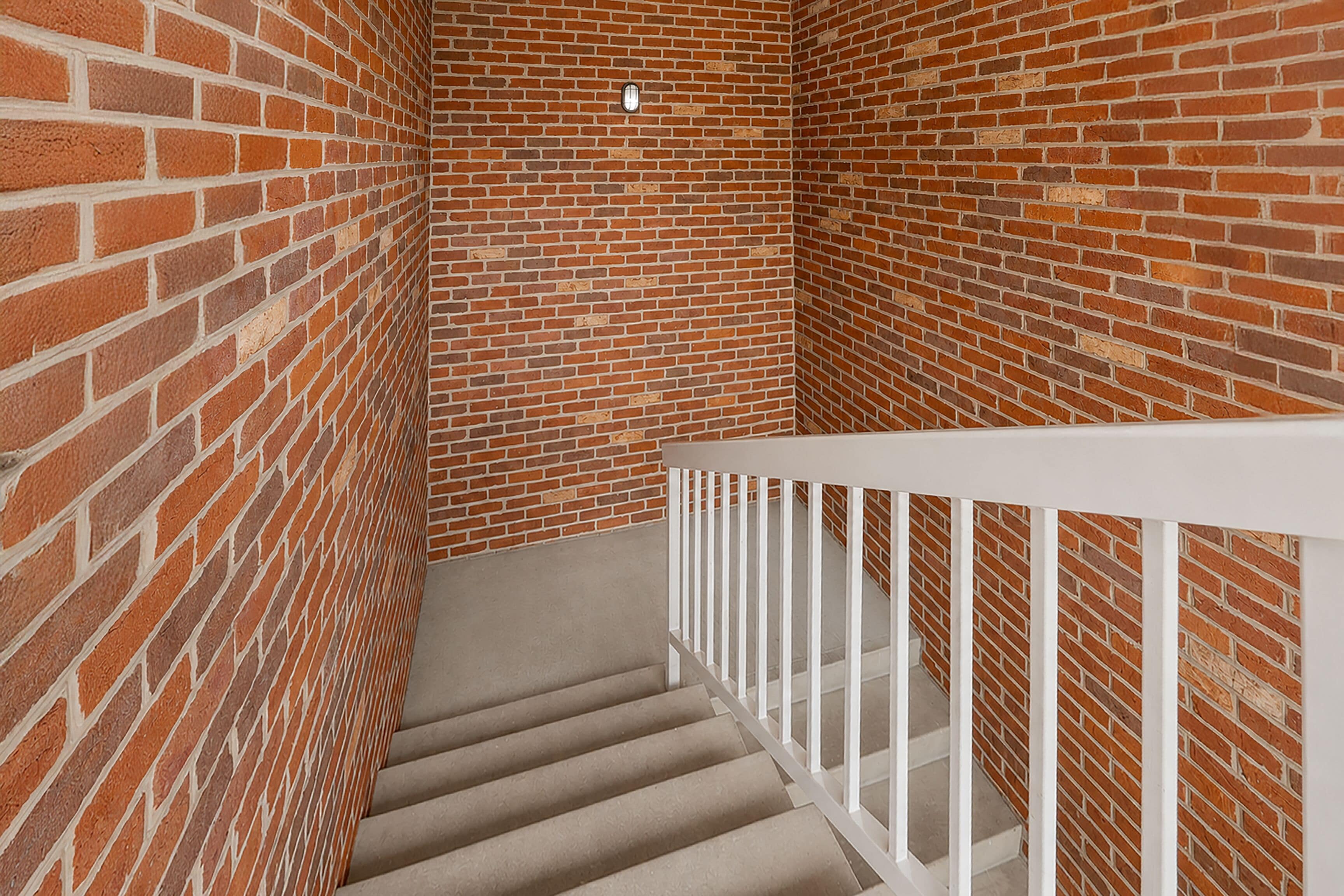 A staircase with a white railing, surrounded by brick walls.