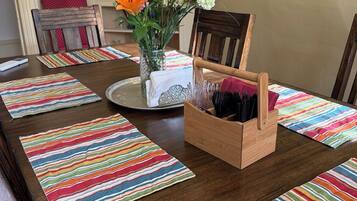Uma mesa de jantar com jogos americanos listrados, um vaso com flores e um suporte de utensílios de madeira.