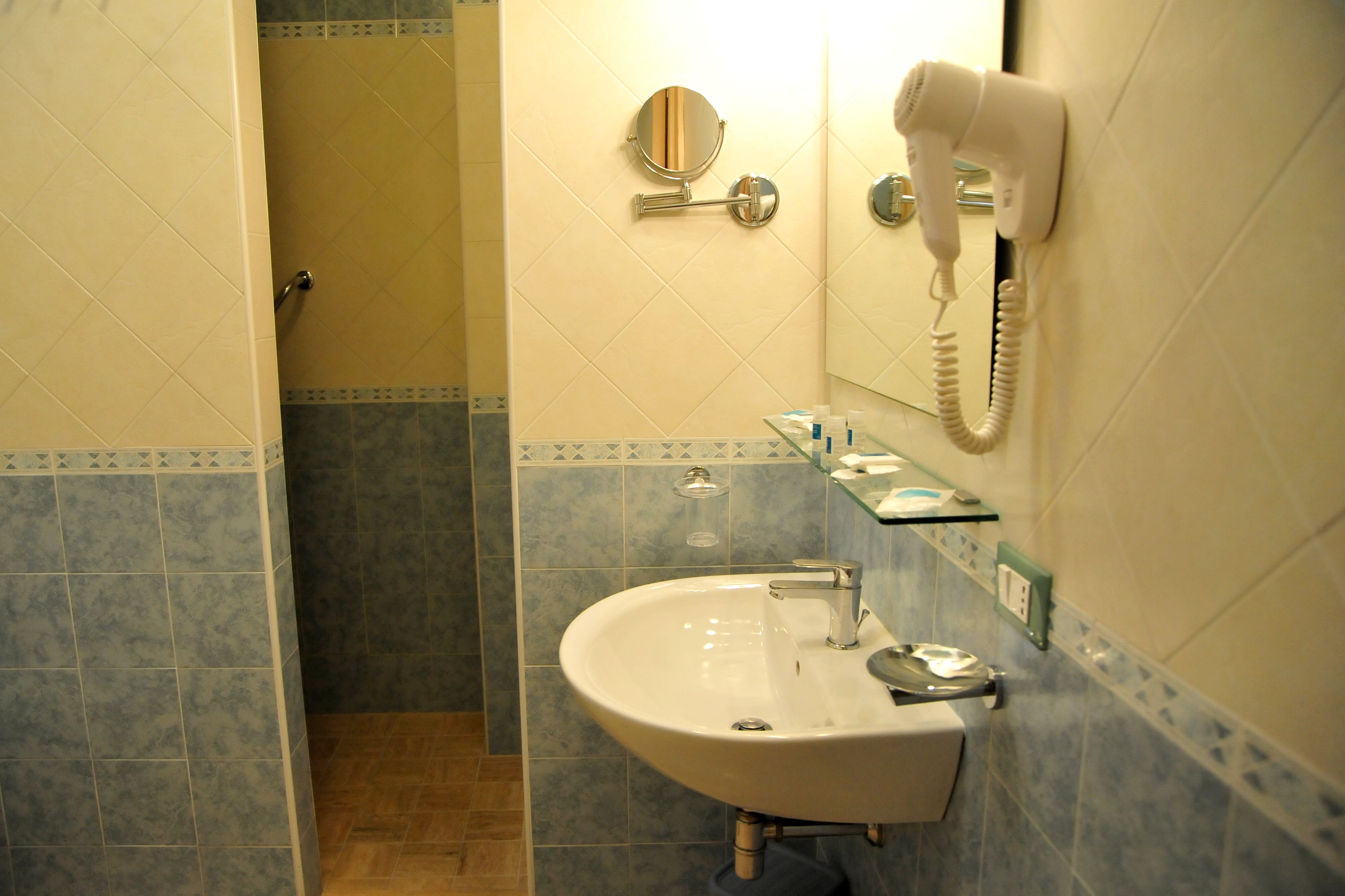 Casa de banho com lavatório, espelho e secador de cabelo fixado na parede.
