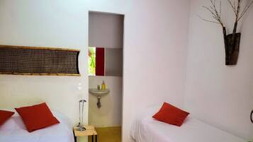 Quarto pequeno e limpo com duas camas, uma mesinha de cabeceira, um espelho e uma pia.