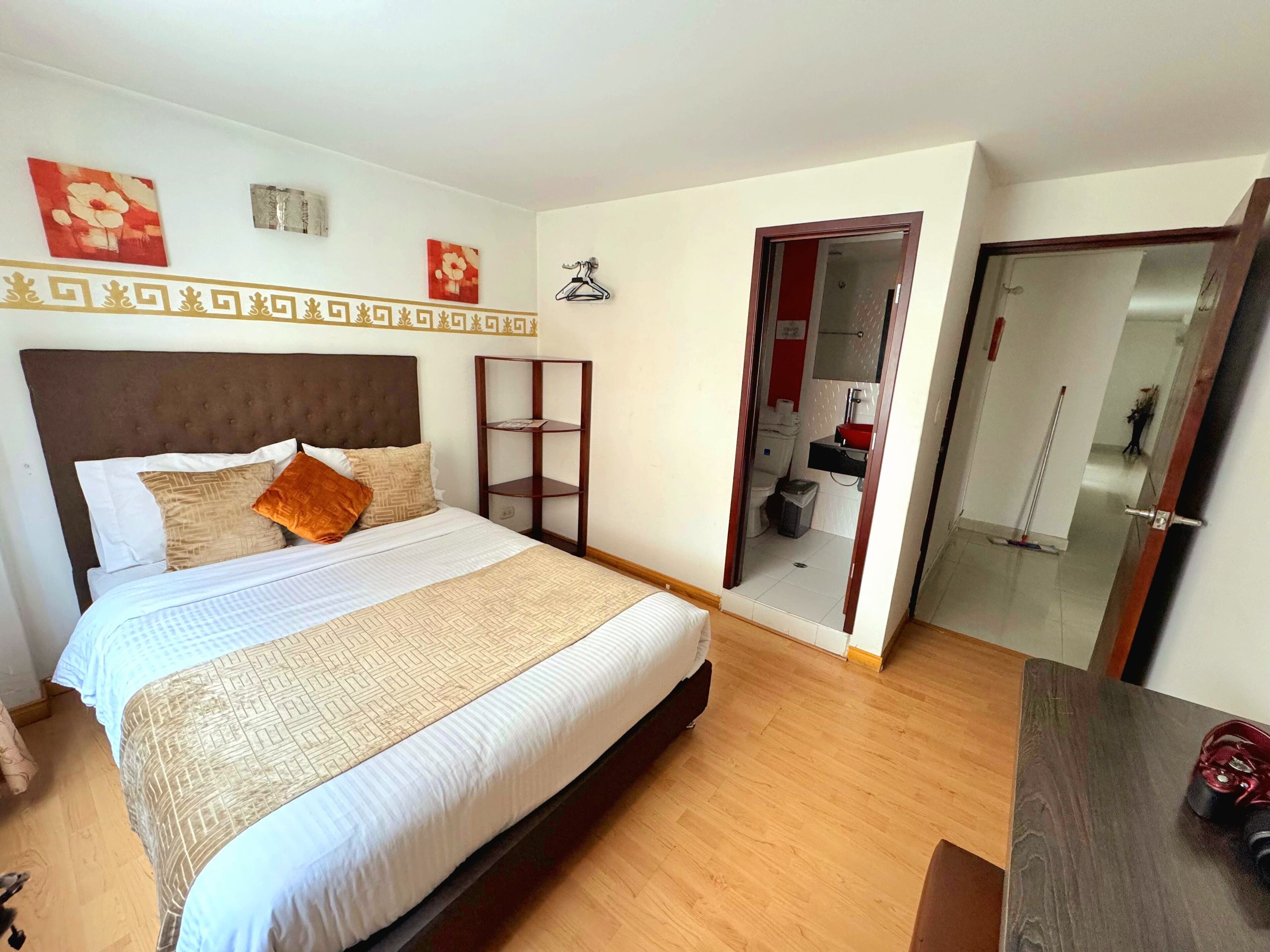 Quarto com uma cama grande, piso de madeira, um pequeno armário e porta para o banheiro.