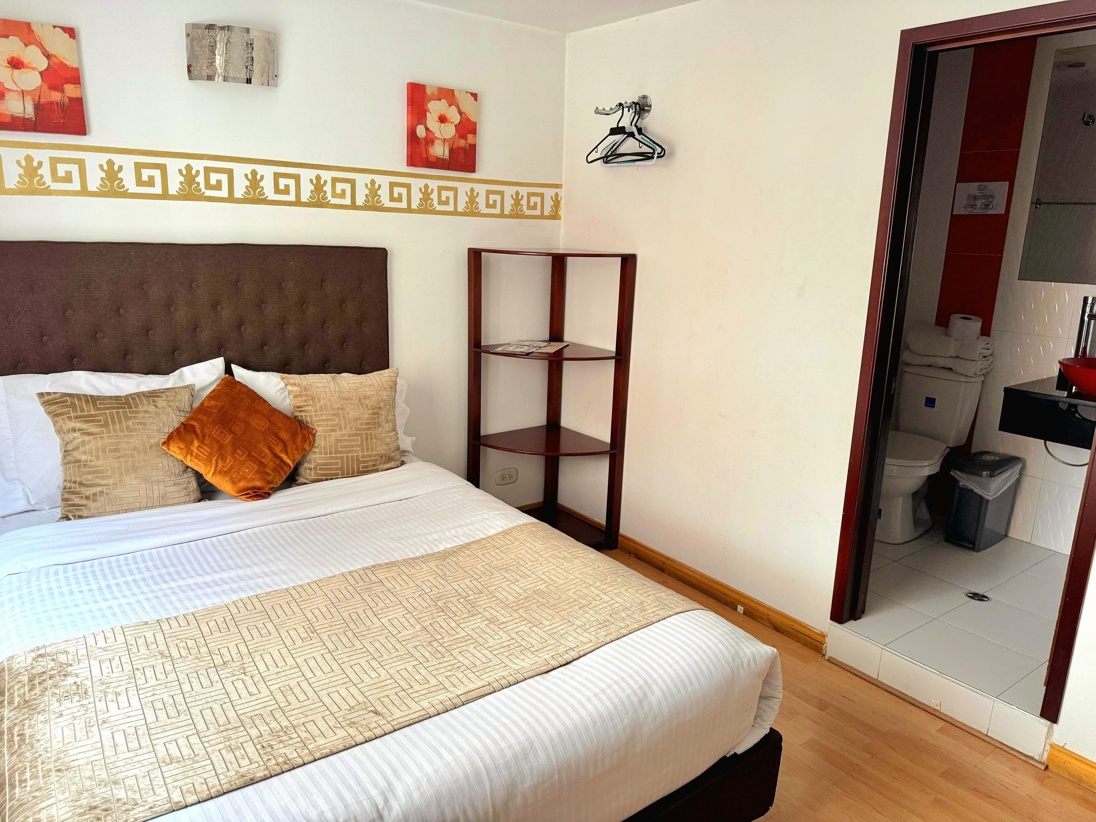 Quarto de hotel bem arrumado com uma cama grande, uma mesa de cabeceira, um espelho e uma pequena prateleira.