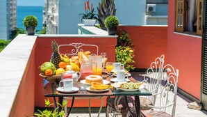 Mesa posta com itens de café da manhã, vista para o mar e plantas em vasos.