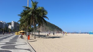 Uma praia com um calçadão, palmeiras e uma montanha ao fundo.
