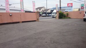 Um parque de estacionamento com entrada por portão, alguns carros estacionados e um edifício com sinalização numa língua estrangeira.