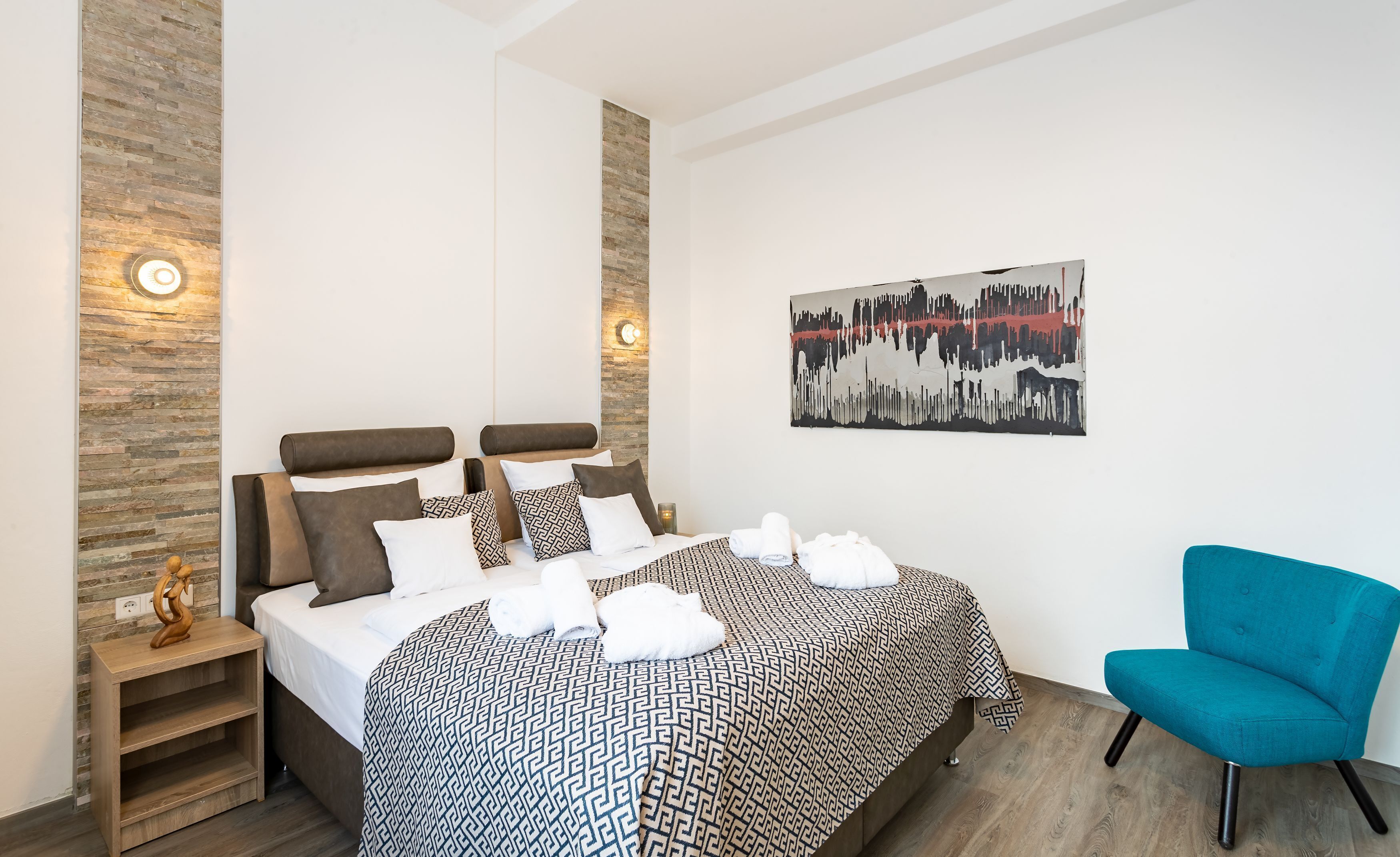 Quarto de hotel moderno com uma cama grande, uma poltrona azul e uma obra de arte urbana na parede.