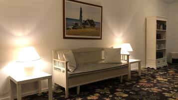 Um quarto com uma cama branca, duas luminárias de cabeceira, um quadro emoldurado de um farol, uma estante branca e um tapete floral.