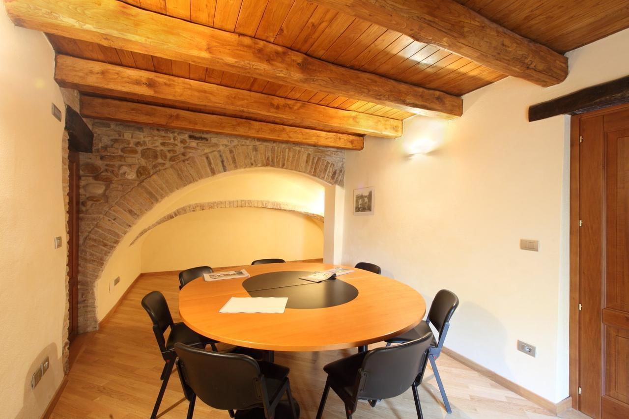 Sala de conferência com uma mesa de madeira redonda, cadeiras pretas e um arco de pedra.
