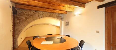 Sala de conferência com uma mesa de madeira redonda, cadeiras pretas e um arco de pedra.