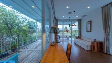 Sala moderna com mesa de jantar de madeira, sofá e uma janela grande com vista para áreas verdes.