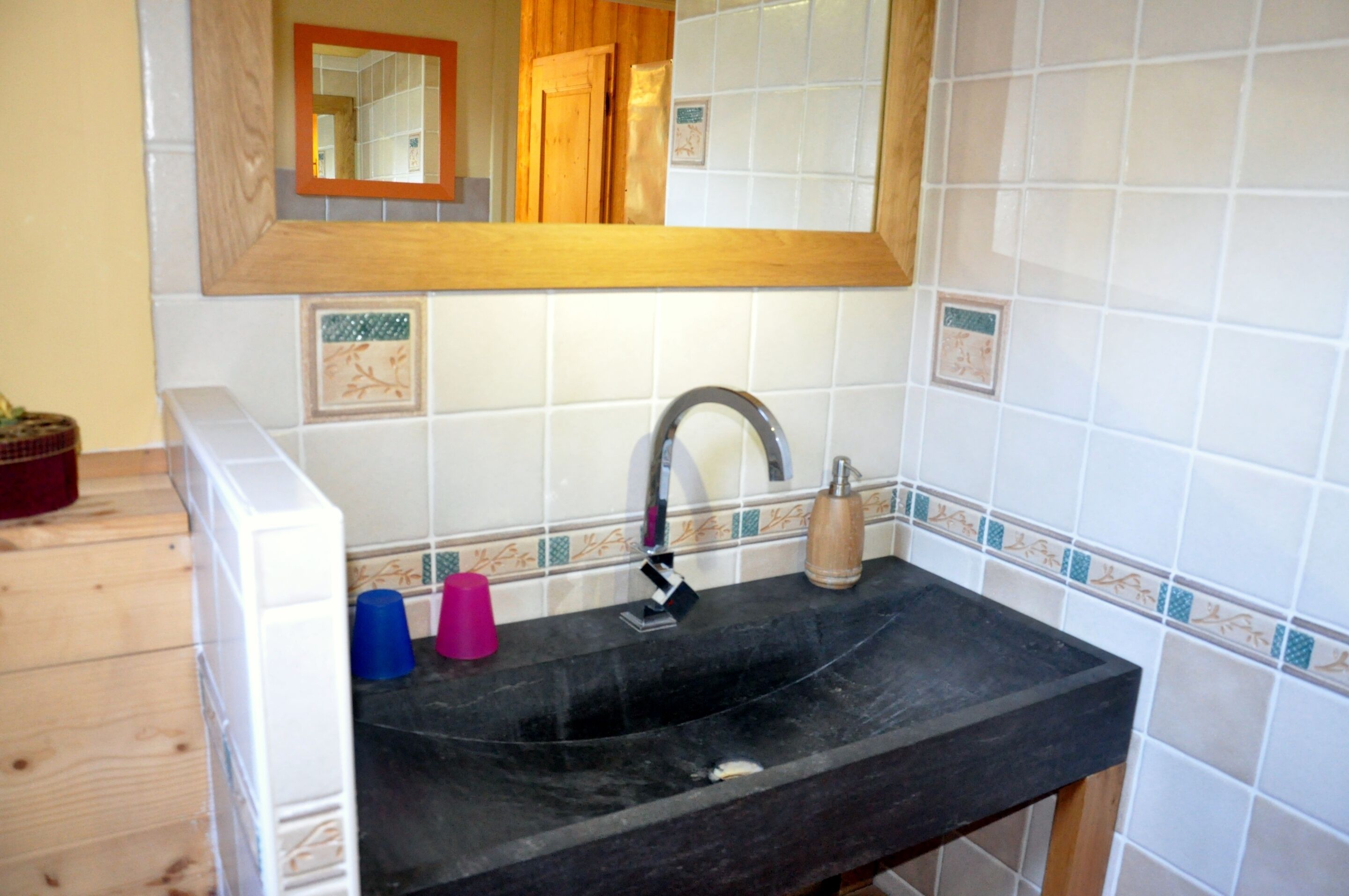 Casa de banho com lavatório preto, bancada de madeira, espelho e paredes com azulejos.