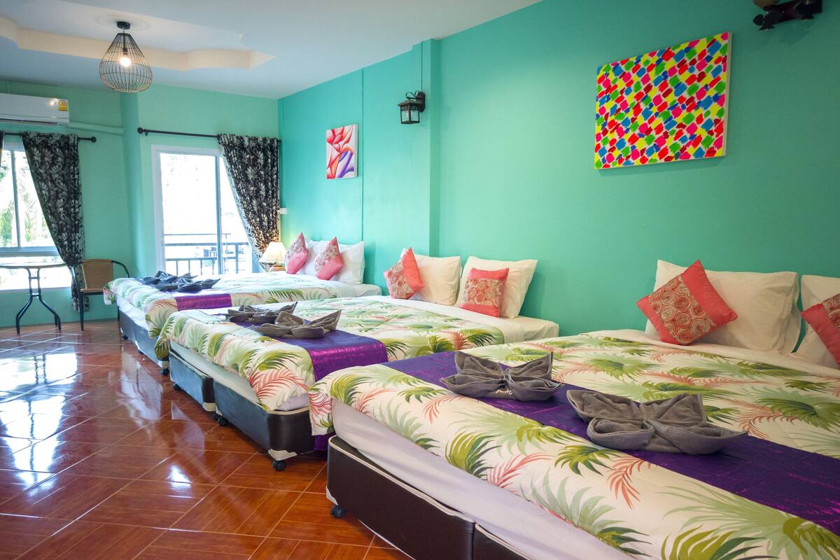 Quarto de hotel com duas camas, janela com cortinas, uma cadeira e uma obra de arte colorida na parede.