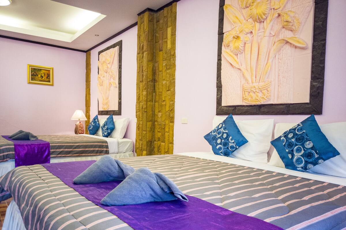 Quarto de hotel com duas camas, cada uma com roupa de cama listrada e almofadas, um cobertor roxo e uma obra de arte pendurada na parede.