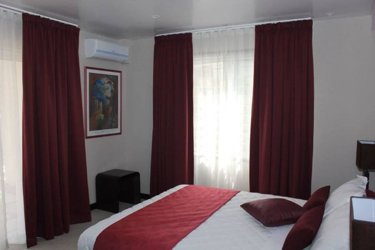 Quarto de hotel com cama grande, cortinas vermelhas, secretária pequena e um quadro na parede.